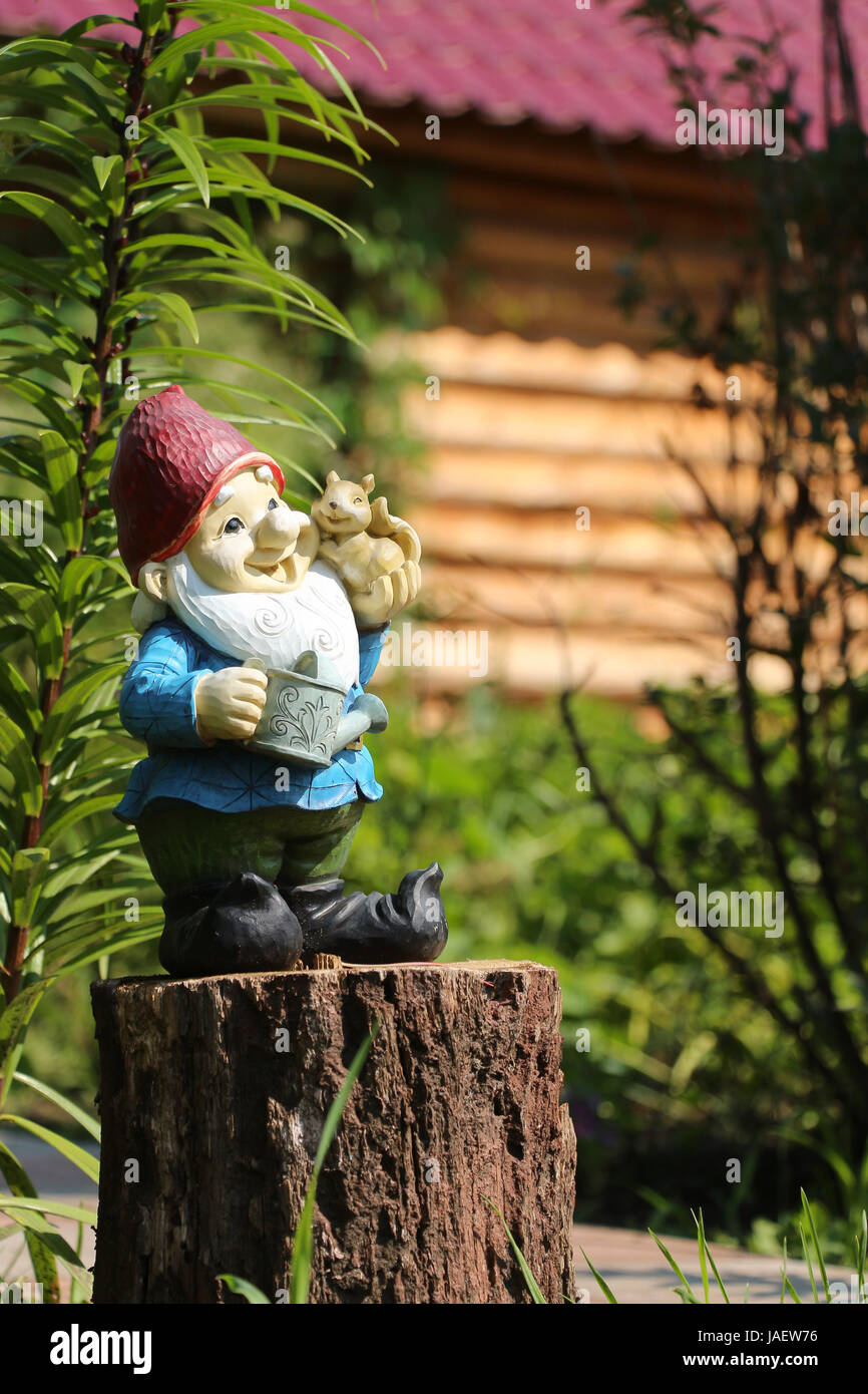 Little garden gnome figurine standing on a tree stump in the backyard ...