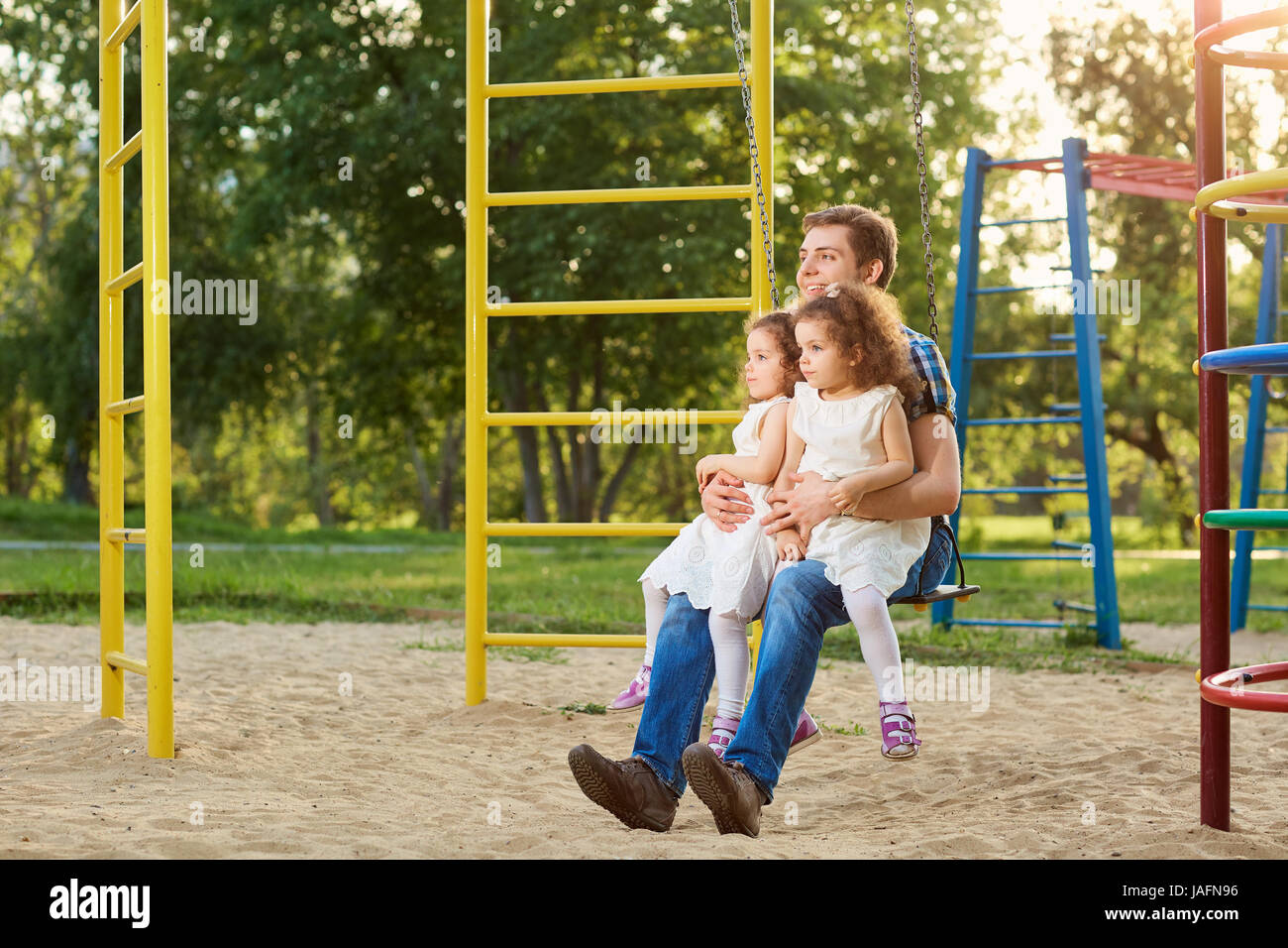 Father with children playing on a swing at the playground Stock Photo ...