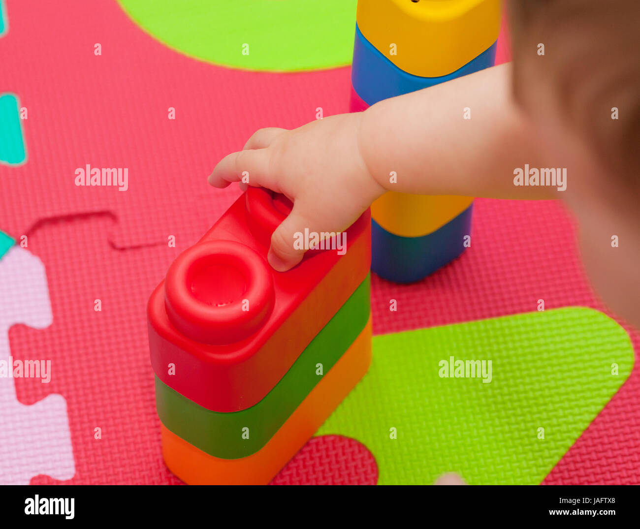 Toddler plays with building block on the colored rubber mat Stock Photo ...