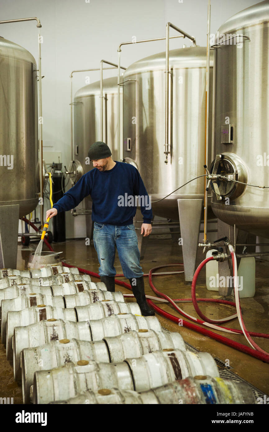 Man standing beside the fermentation tanks, cleaning metal beer kegs ...