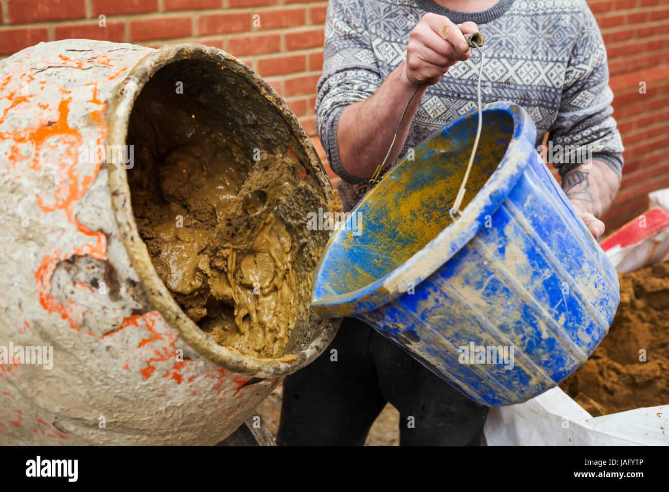 A builder, bricklayer standing next to a cement mixer, holding a blue ...