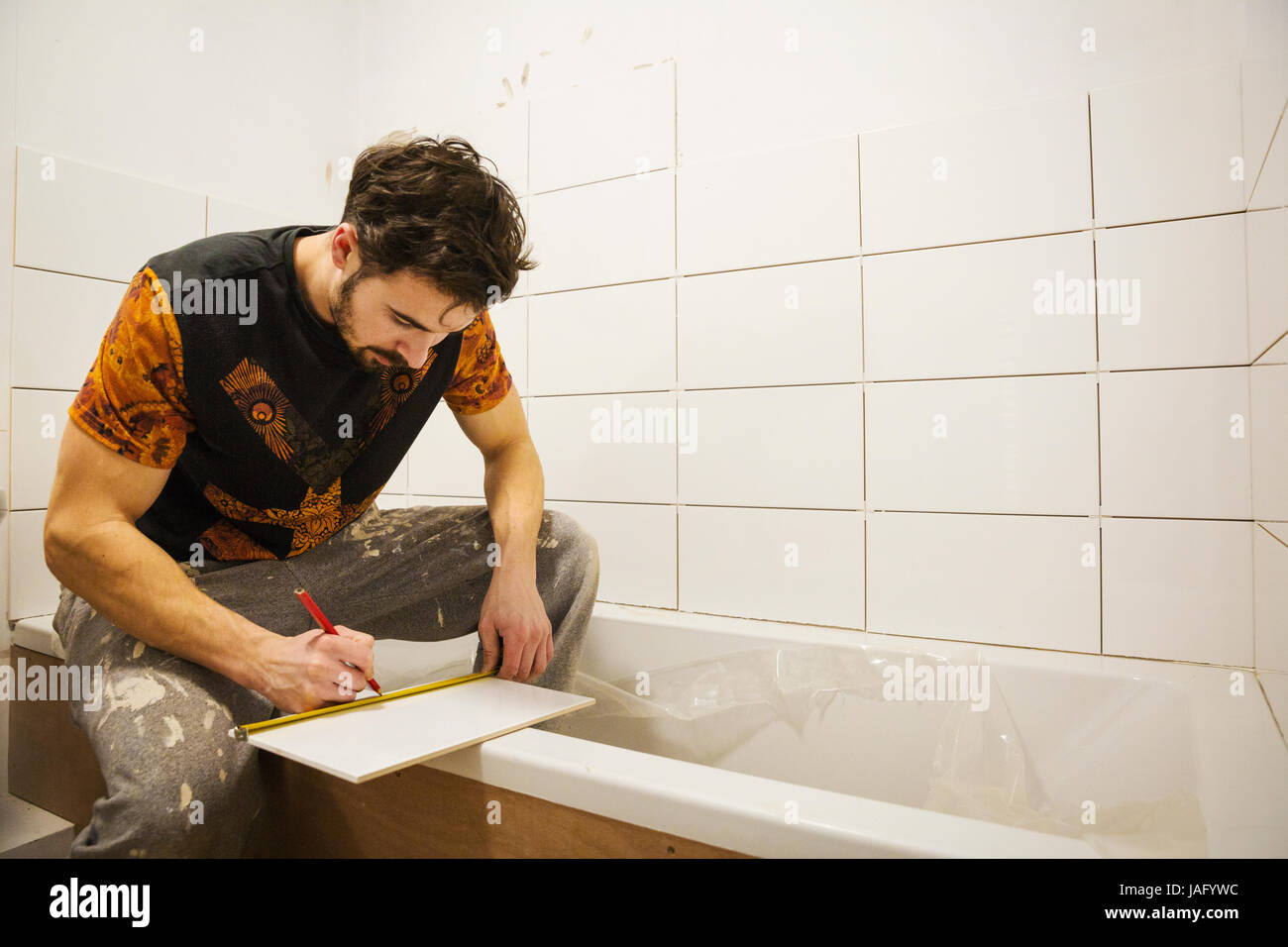 A builder, tiler working in a bathroom, marking a tile with a pencil ...
