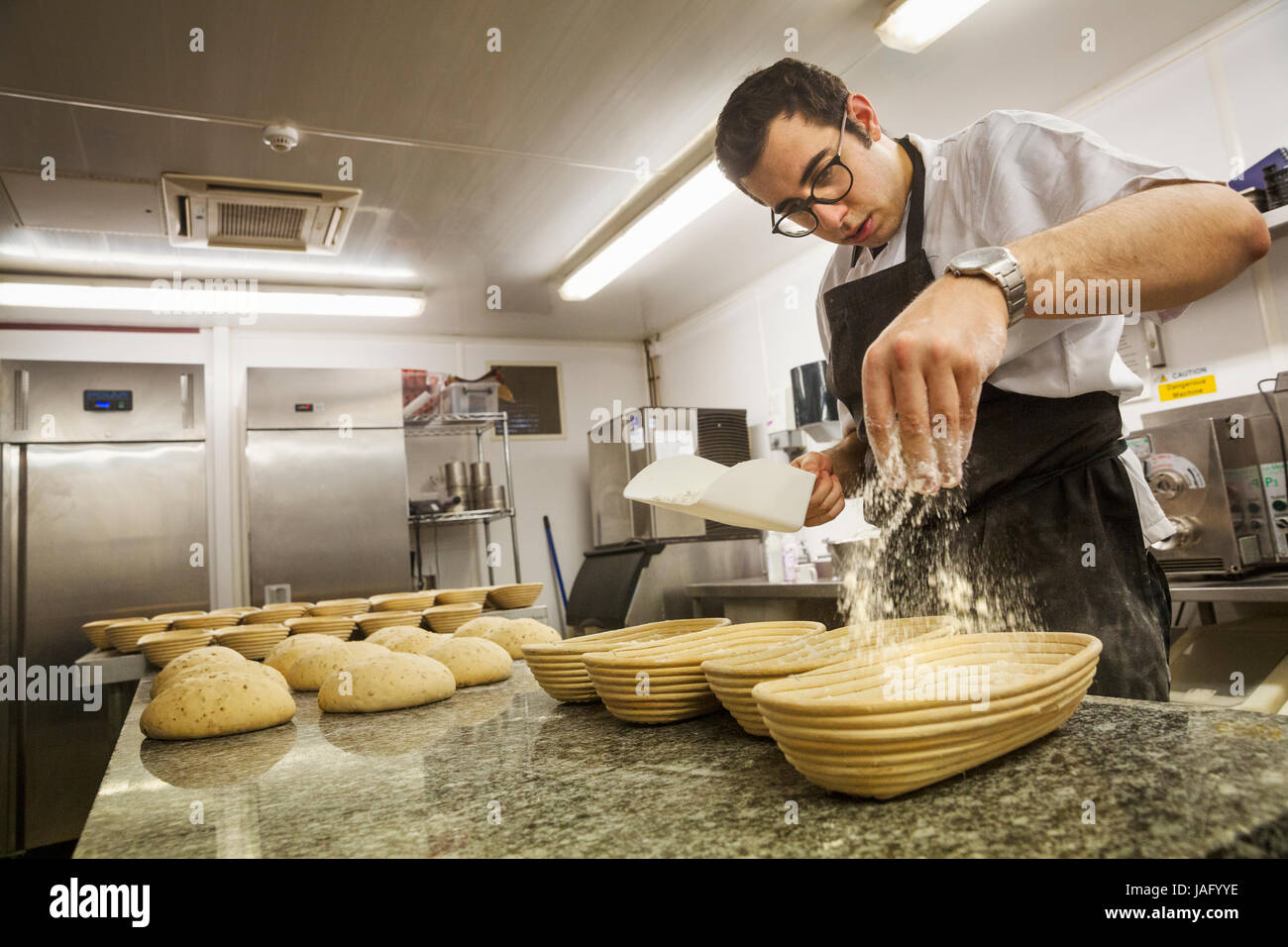 Baker sprinkling flower on bread dough and proving baskets in the ...