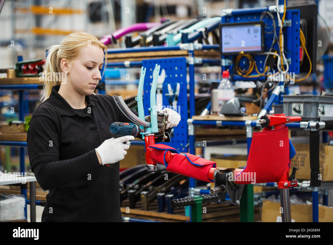 Female skilled factory worker assembling a bicycle handling the brakes ...