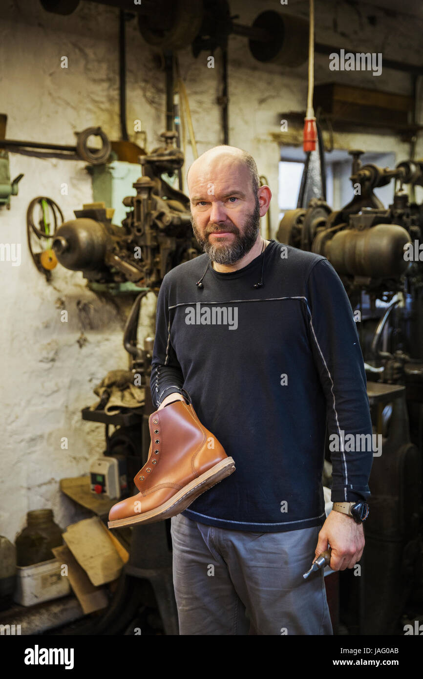 Man standing in a shoemaker's workshop, holding a pair of brown leather ...
