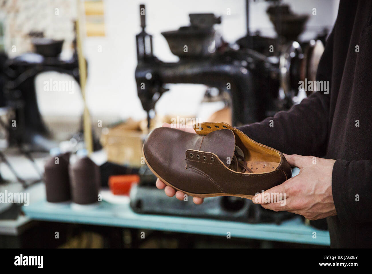 Man standing in a shoemaker's workshop, holding brown leather shoe ...