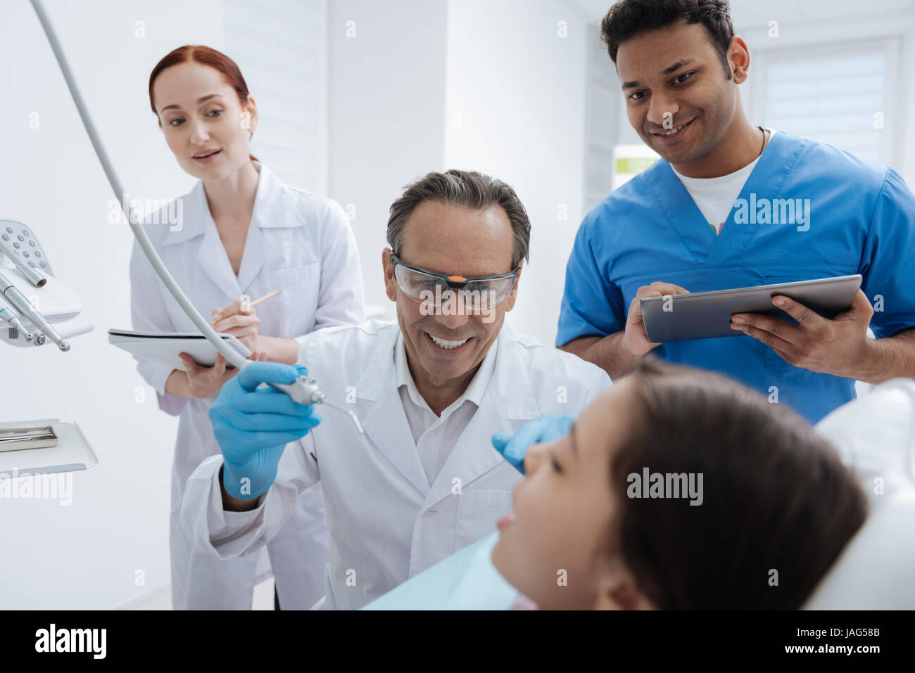 Little patient. Joyful dentist keeping smile on his face and wearing ...