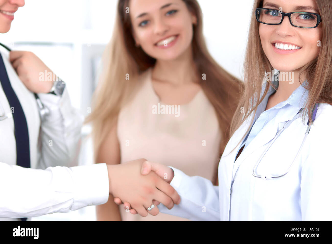 Two doctors shaking hands to each other while patient standing near ...