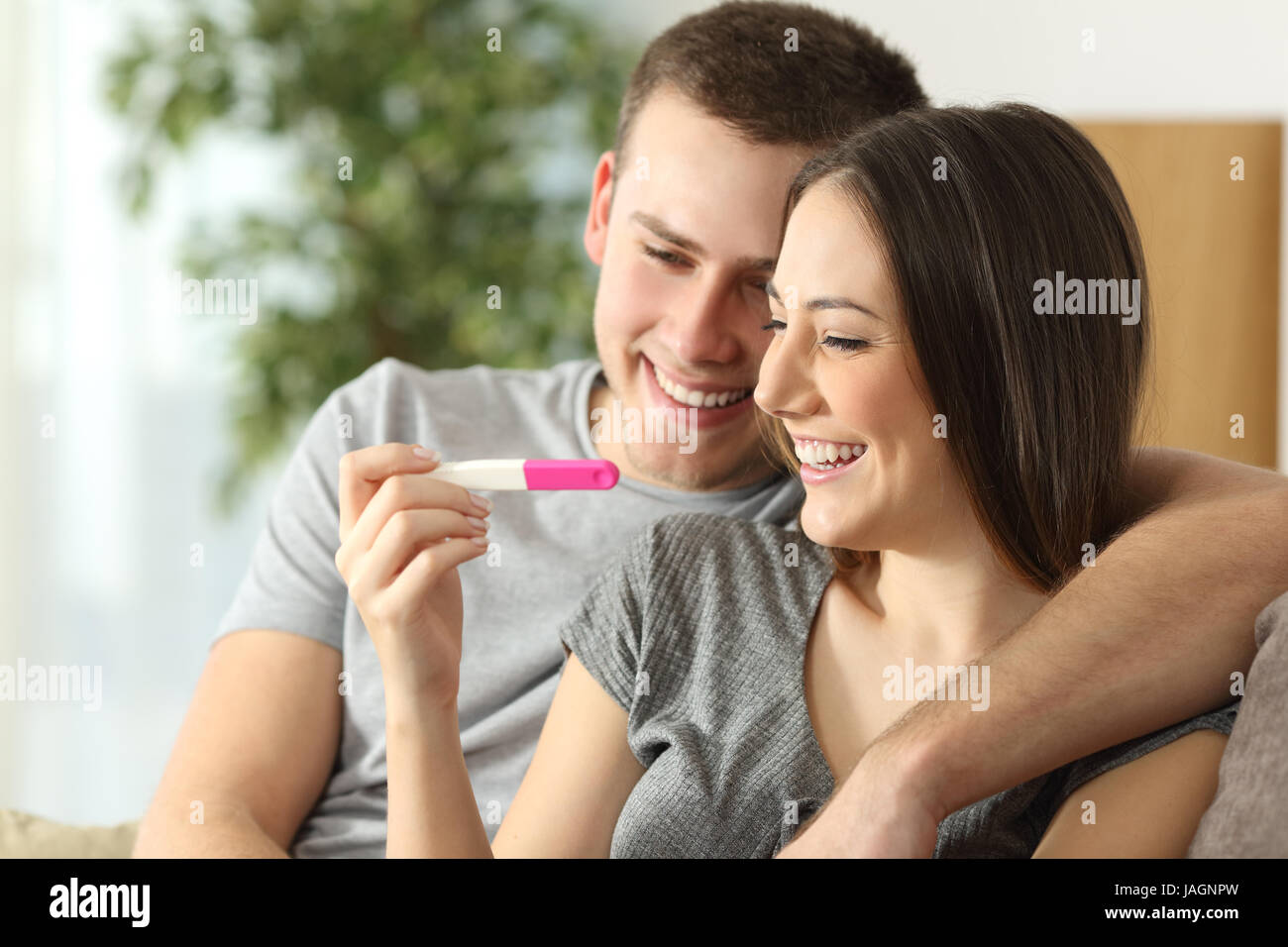 Happy couple checking pregnancy test sitting on a couch in the living ...