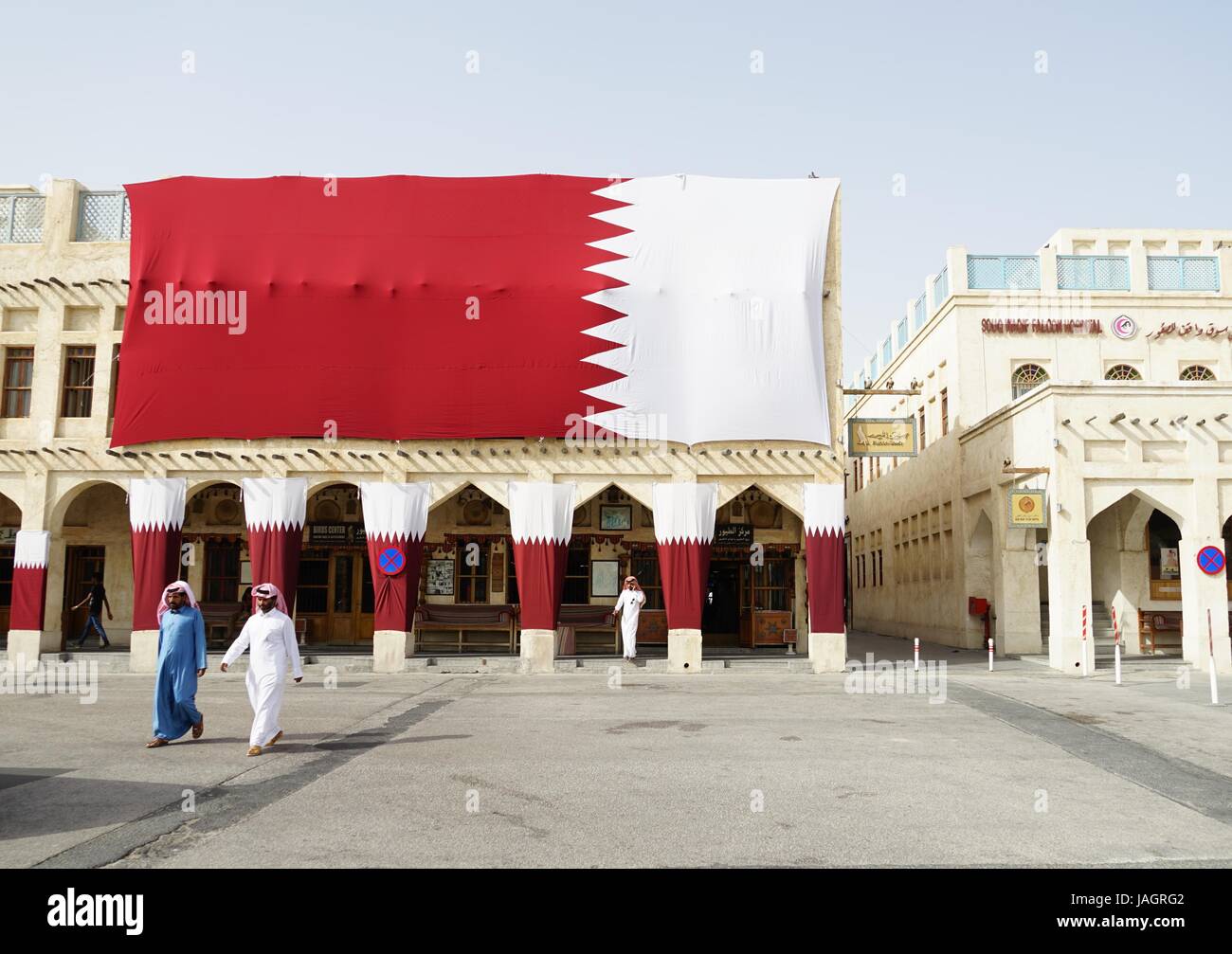 Two Qatari men in traditional robes walking near the Souq under a giant ...