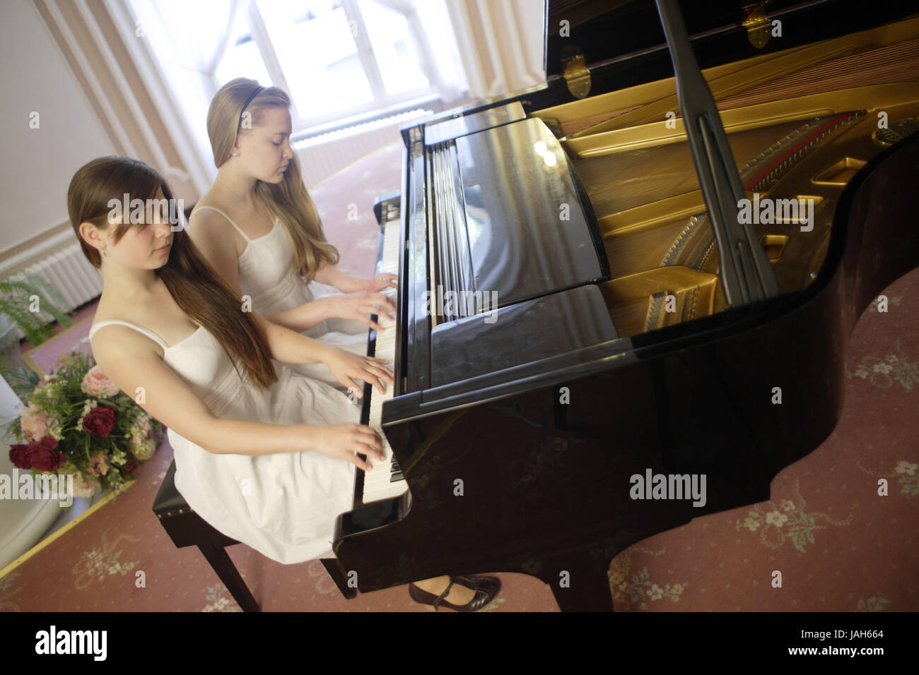 Two girls in white clothes play together the piano Stock Photo - Alamy