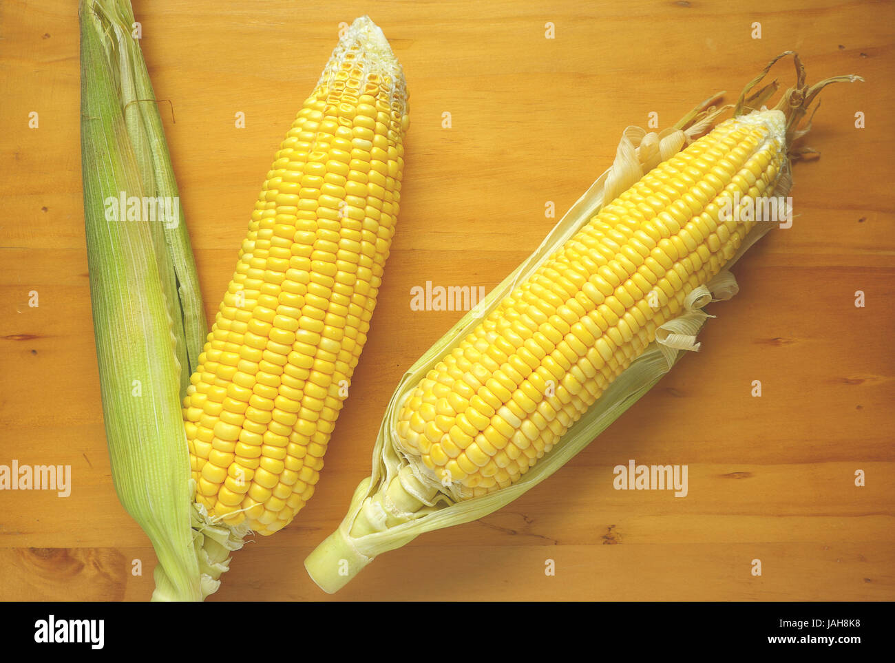 Fresh ripe sweet corns and green corn husks. On wooden background Stock ...