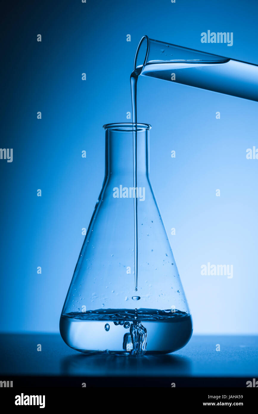 Filling a Erlmeyer flask from a reagent glass against blue toned studio ...