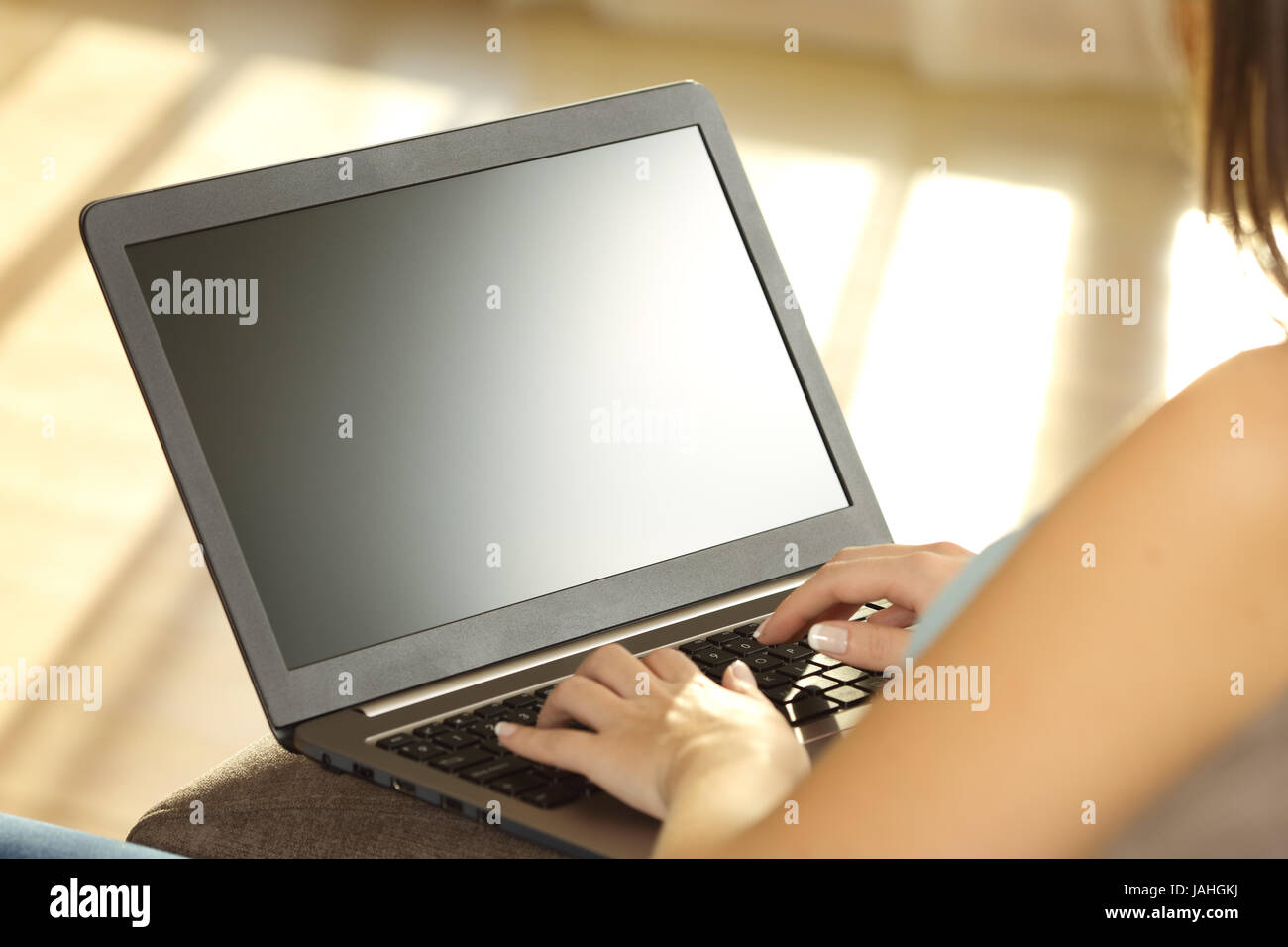 Girl using laptop and showing a blank monitor sitting on a couch in the ...