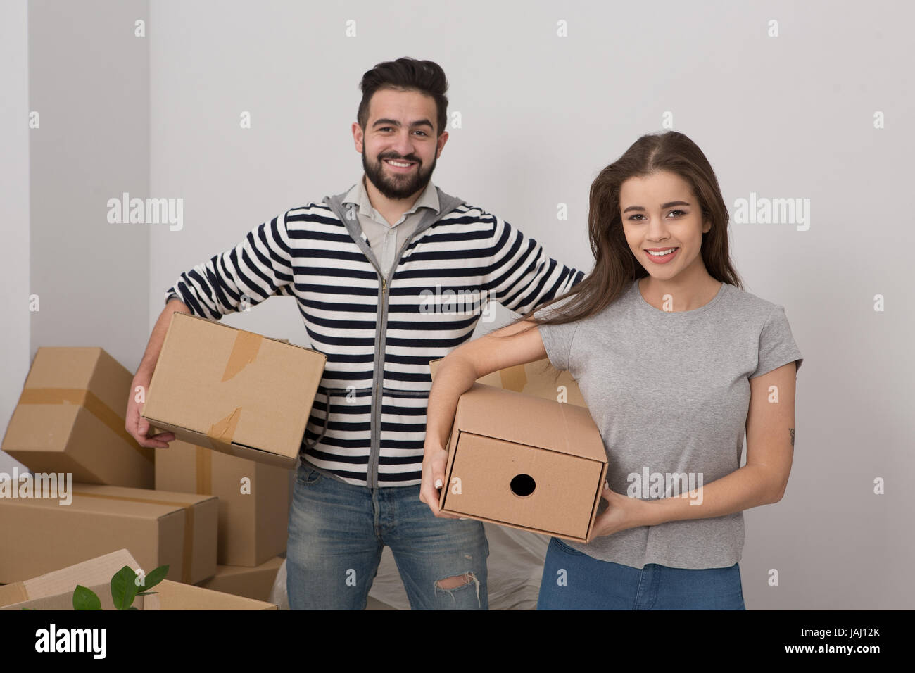 Attractive young couple is moving, smiling and holding boxes while ...