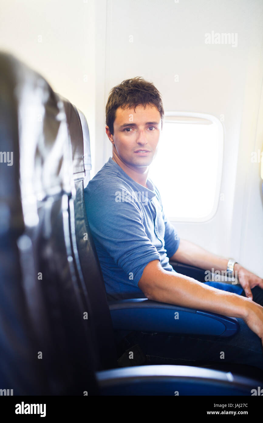 Handsome young man on board of an airplane during flight, looking at ...