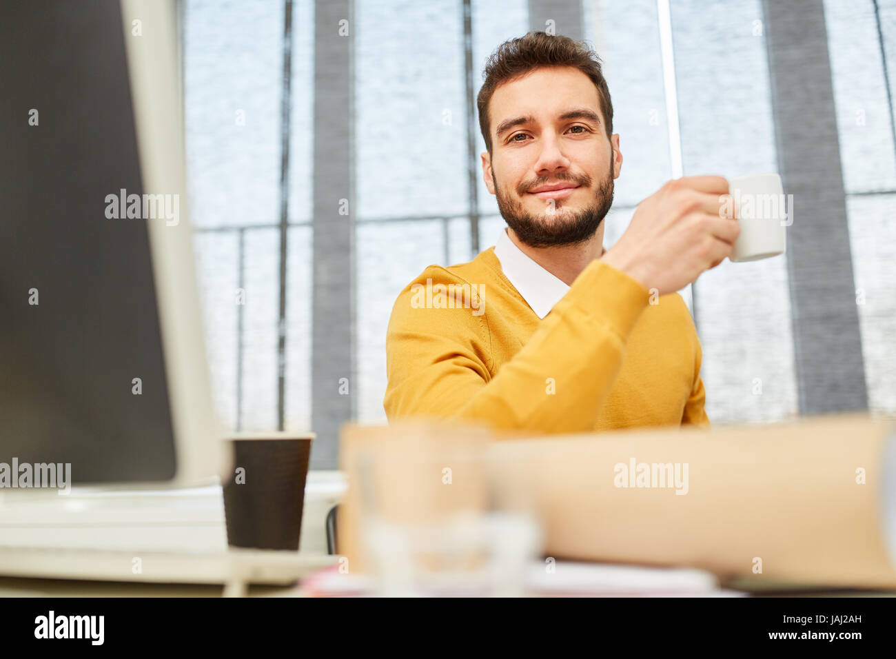 Young man drinking a cup of coffee at his place of work Stock Photo - Alamy