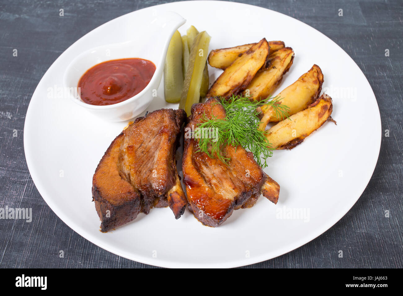 Roast pork ribs with potatoes and pickles. Plate located on a black ...