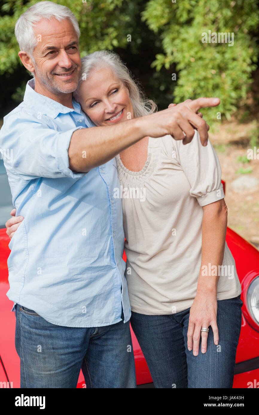 Smiling mature couple posing by their red convertible on bright day ...