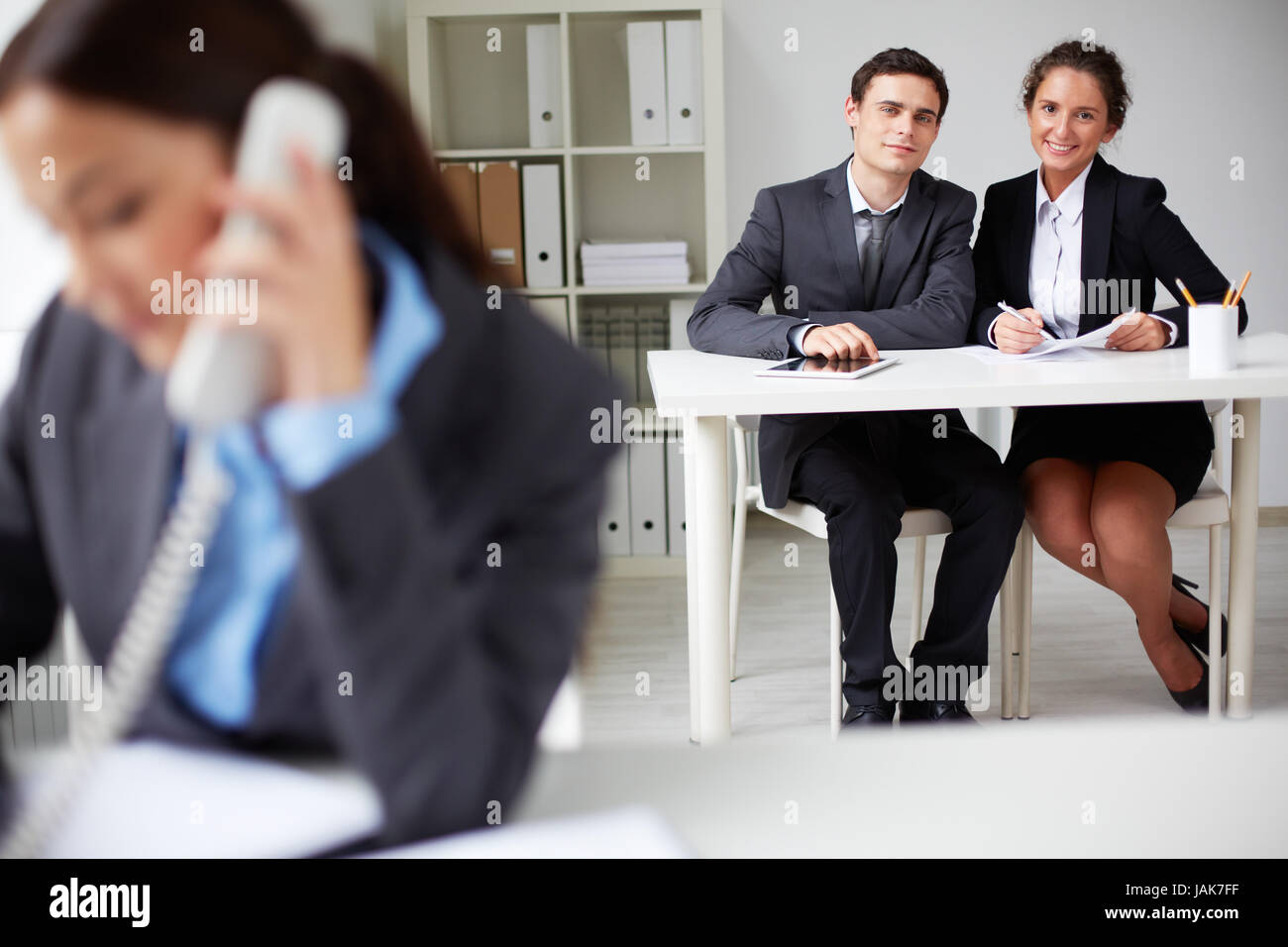 Happy business partners looking at camera with their colleague calling ...