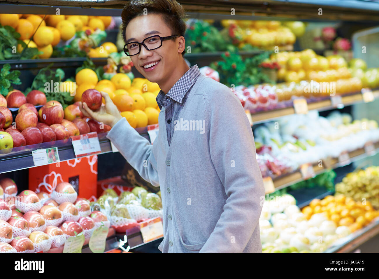 one young asian man picking apple in the suppermarket looking at camera ...
