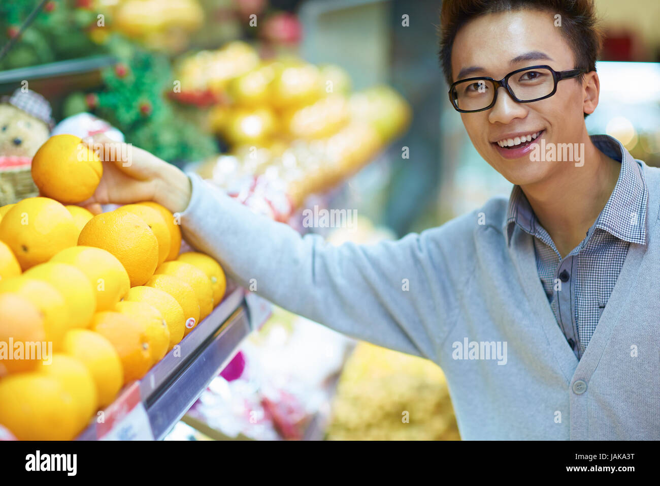 one young asian man picking apple in the suppermarket looking at camera ...
