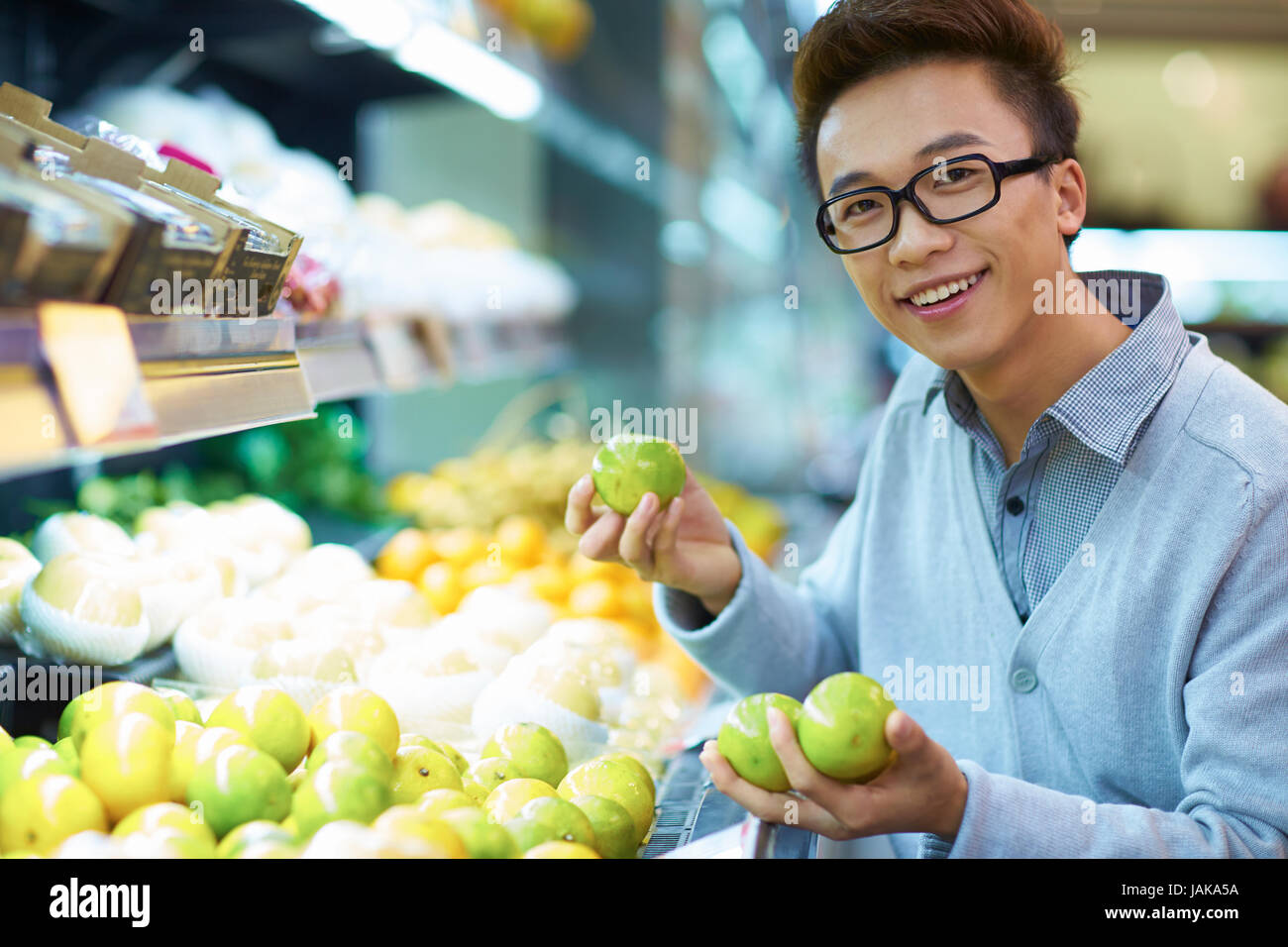 one young asian man picking apple in the suppermarket looking at camera ...