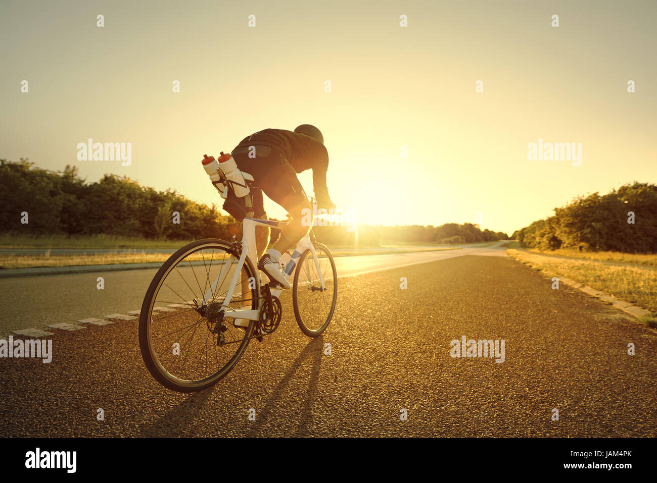 An unrecognizable sportsman on bicycle moving on the empty evening road ...