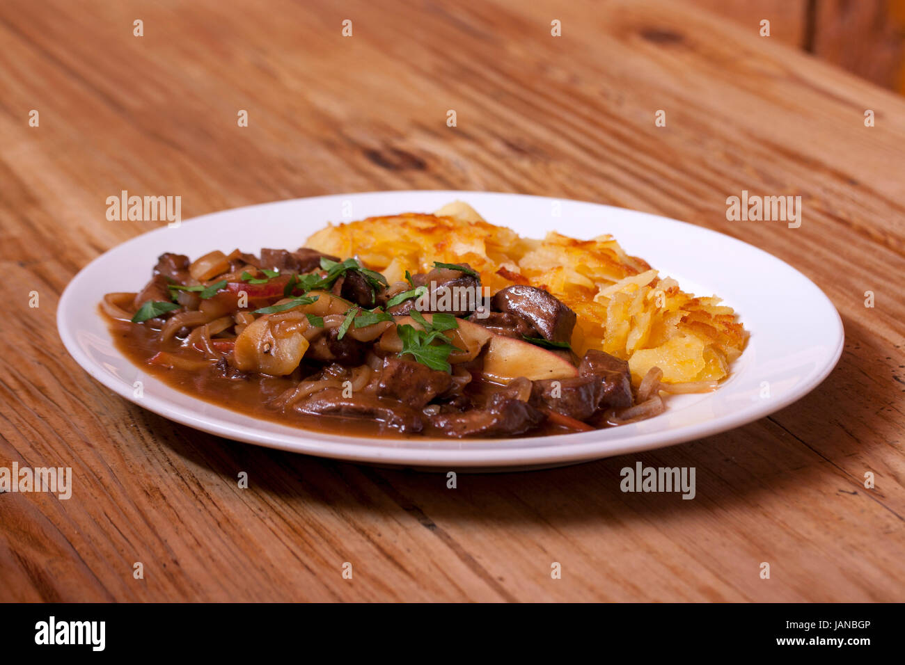 Rehgulasch mit Äpfel und Kartoffelgratin auf Teller mit Holzhintergrund ...