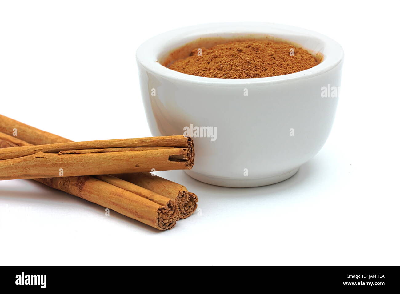 Grounded cinnamon in a bowl with cinnamon sticks on white background ...