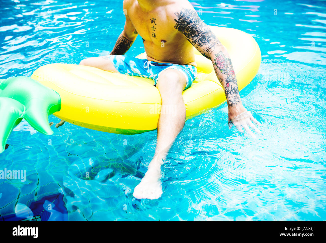 Caucasian tattooed man floating in the swimming pool by inflatable ...