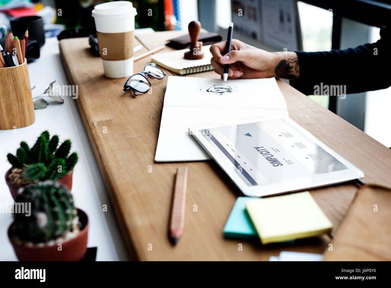 Tattooed hand drawing artwork on wooden table Stock Photo - Alamy
