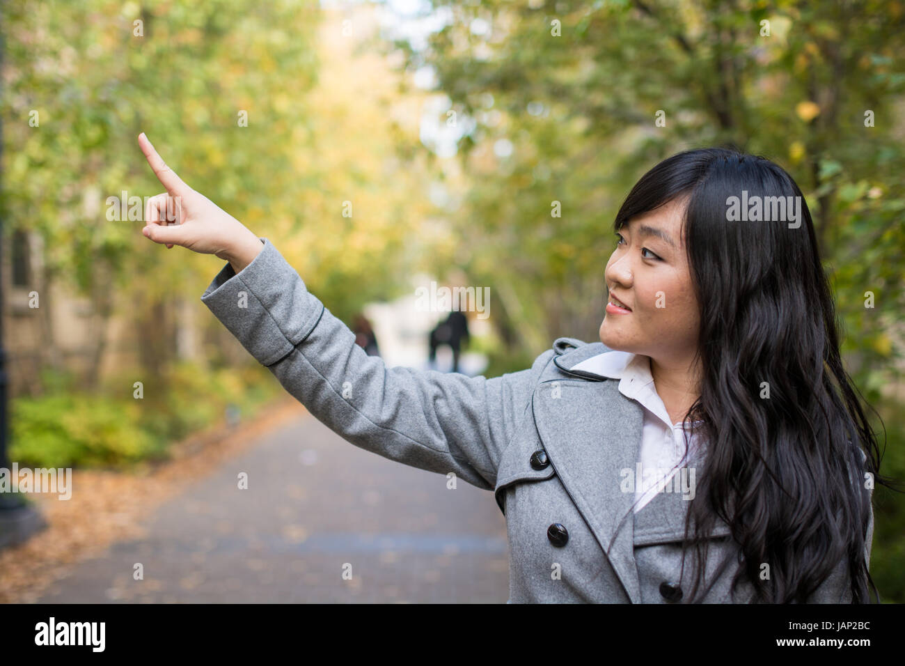 Portrait of young attractive girl pointing at something on the trees at ...