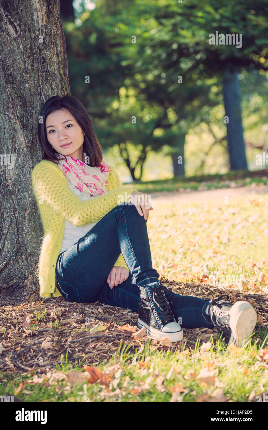 Portrait of happy looking woman sitting against a tree Stock Photo - Alamy