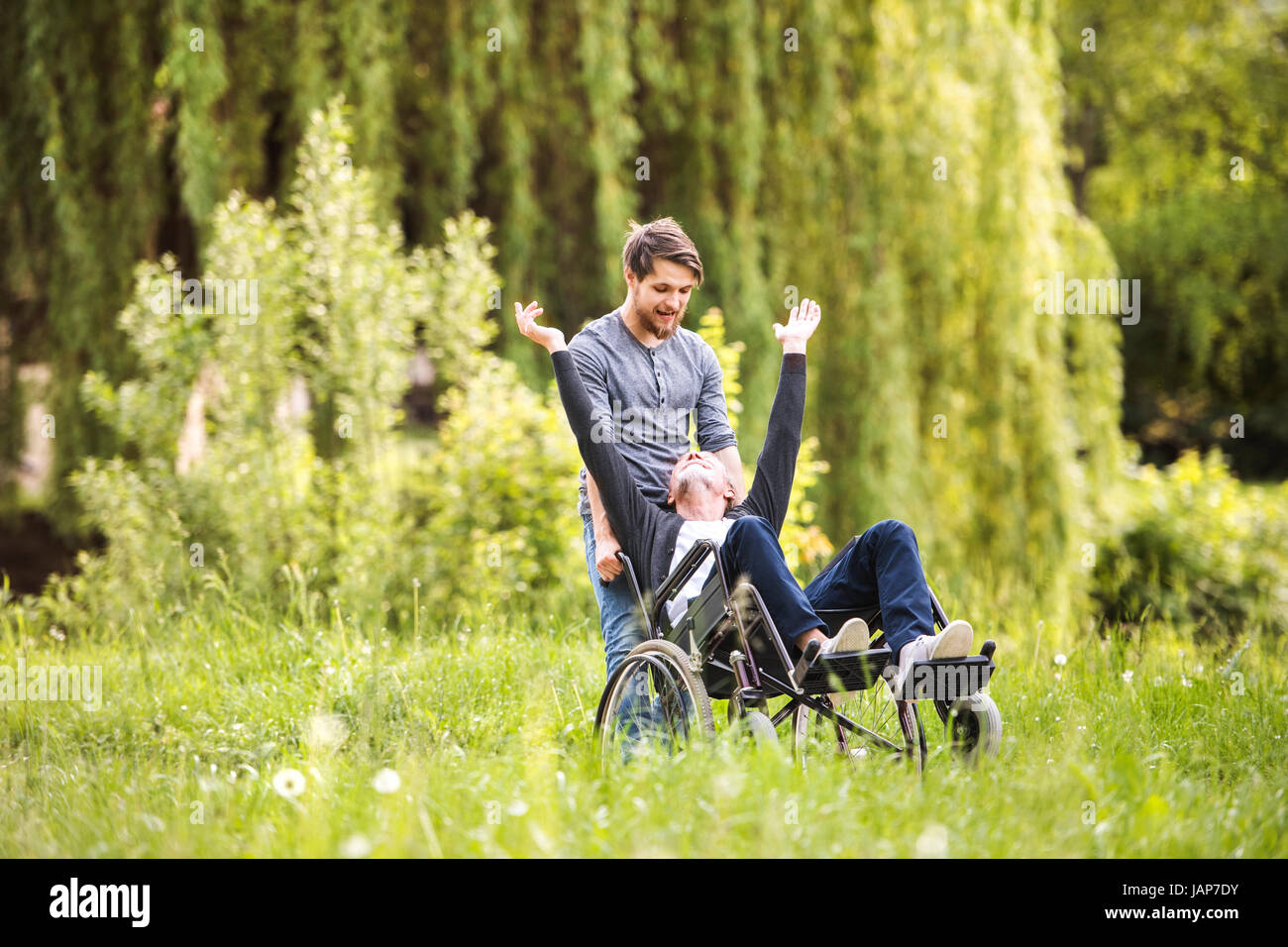 Hipster son walking with disabled father in wheelchair at park Stock ...