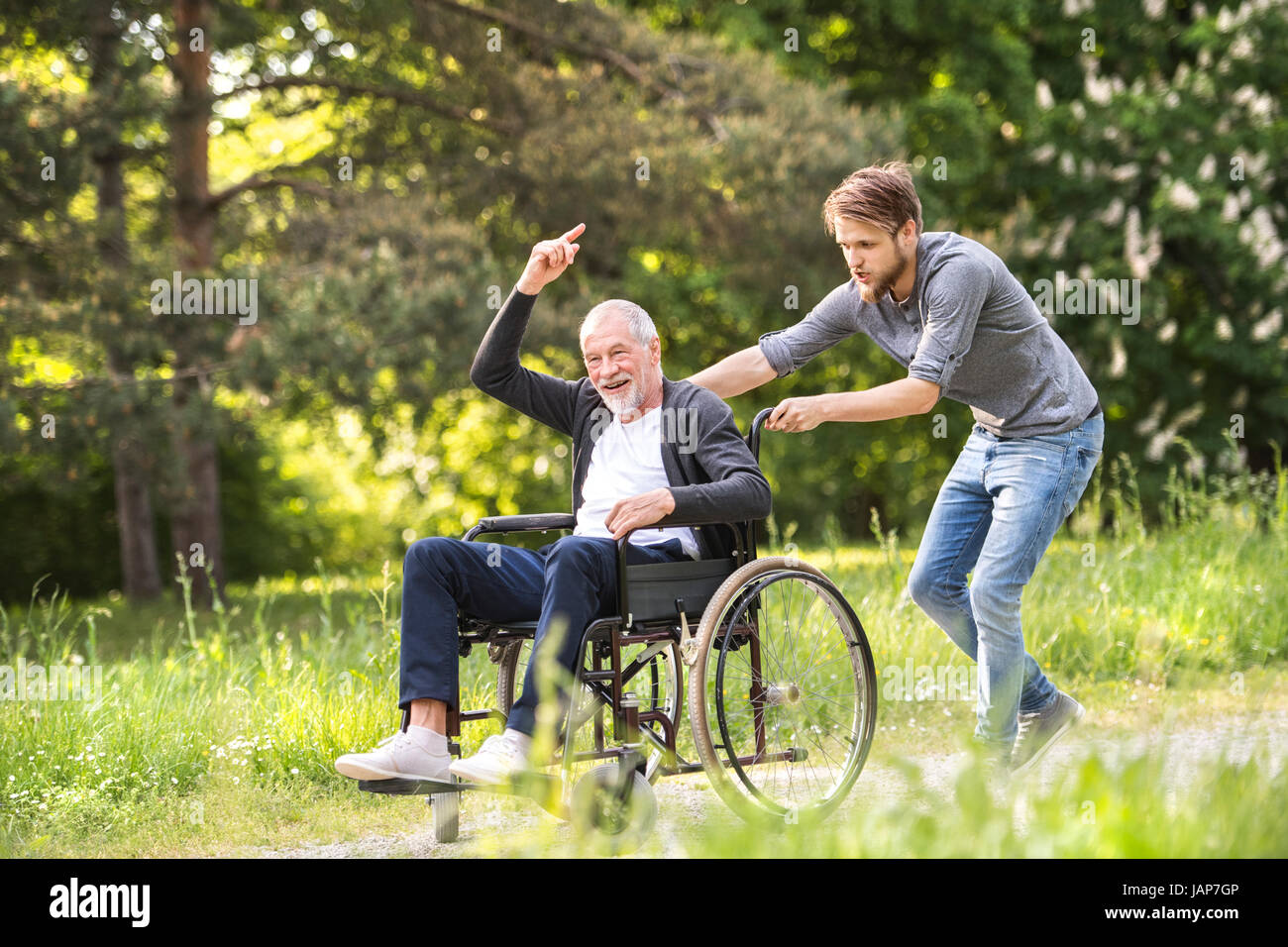 Hipster son walking with disabled father in wheelchair at park Stock ...