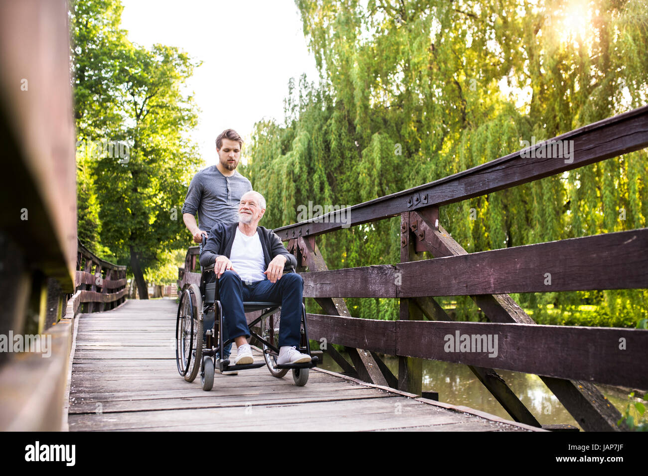 Hipster son walking with disabled father in wheelchair at park Stock ...