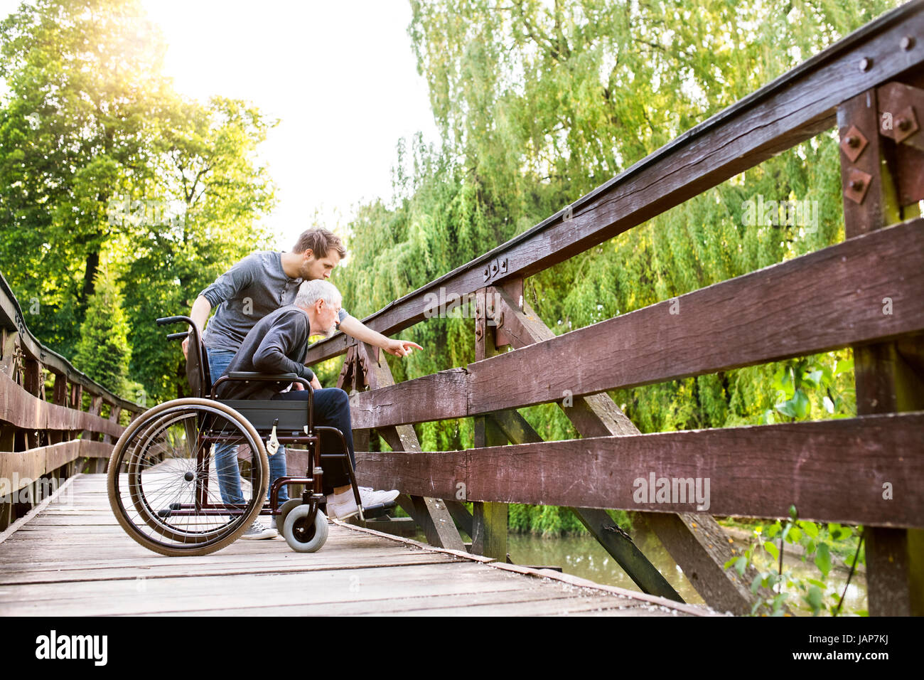 Hipster son walking with disabled father in wheelchair at park Stock ...