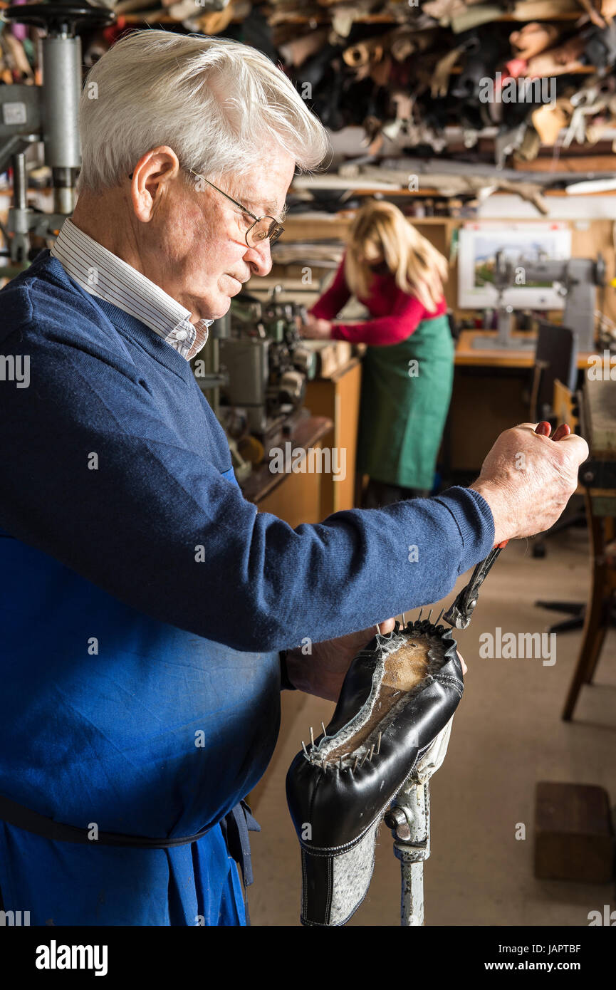 Shoemaker, man pulling nails with pliers out of last, at back woman at ...