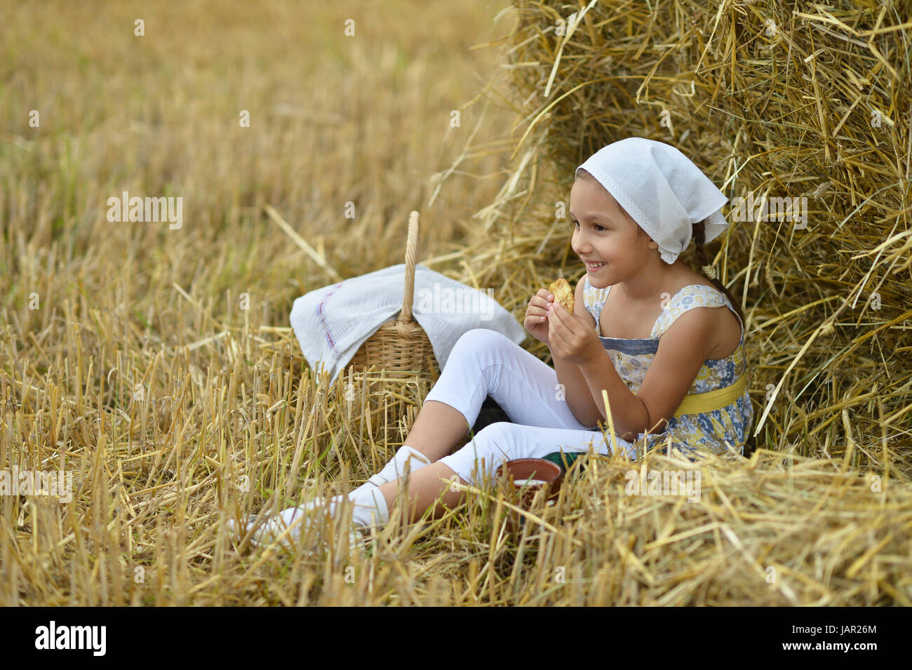 Little girl having lunch while sitting near stack of hay Stock Photo ...