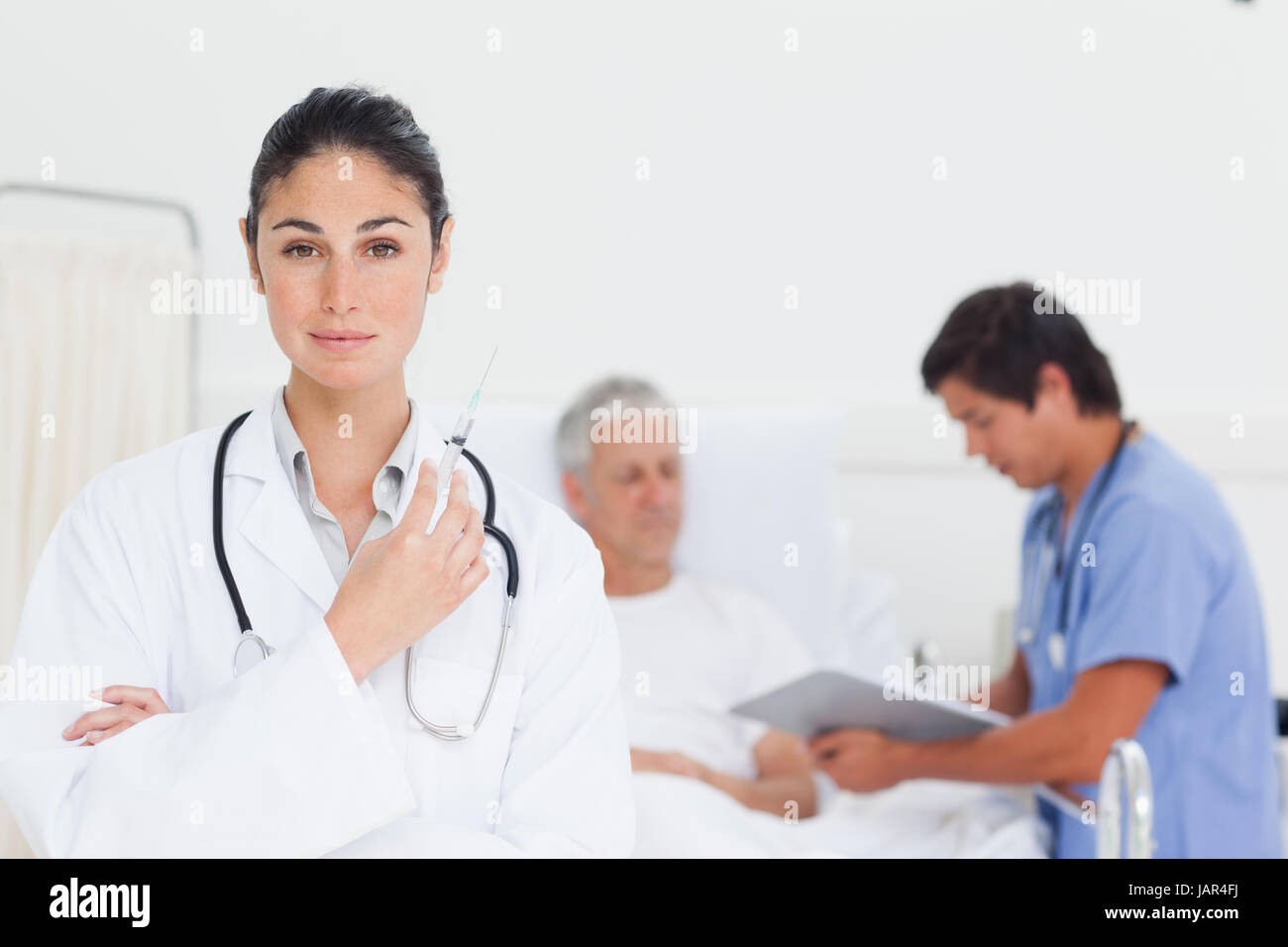 Serious doctor looking ahead while holding a syringe as she stand in ...
