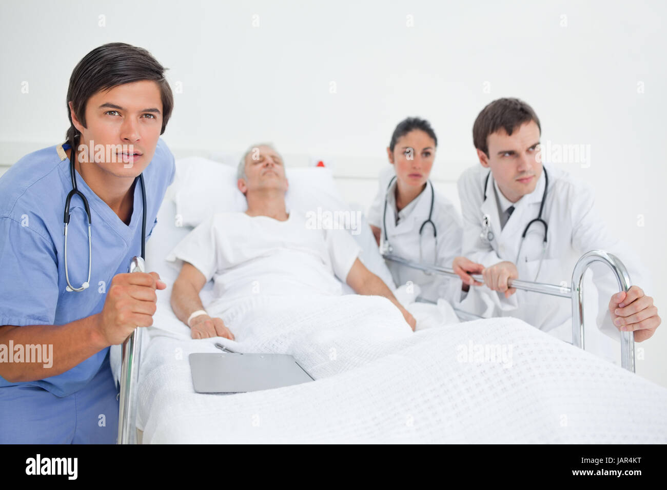 Nurses and doctors with serious expressions pushing a hospital bed with ...