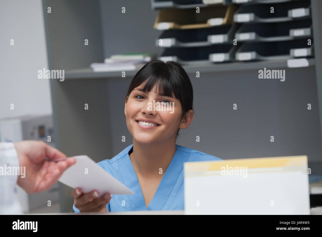 Nurse smiling while holding a paper while sitting behind a hospital ...