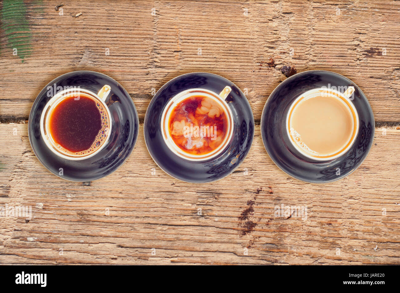 Three cups of coffee with black, white and flowing milk on wooden ...