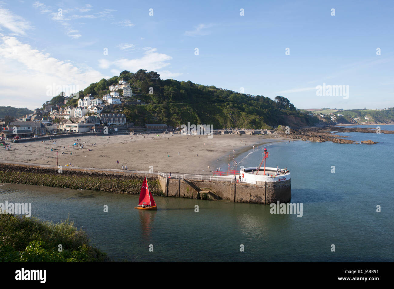 A dinghy with a red sail heads out to sea past the banjo pier at Looe ...