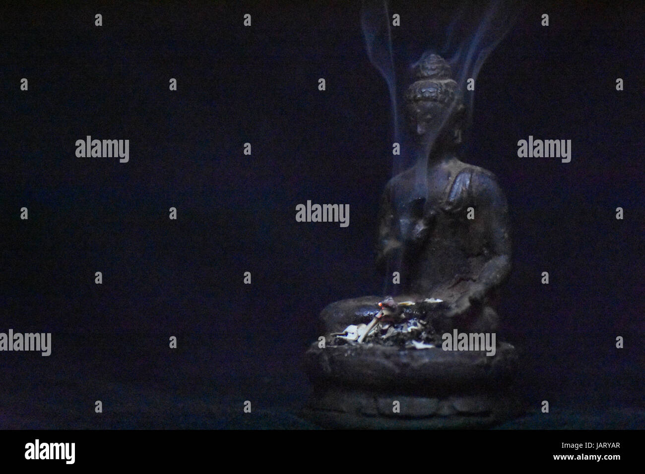 Buddha statue with incense smoke swirling against a dark background ...