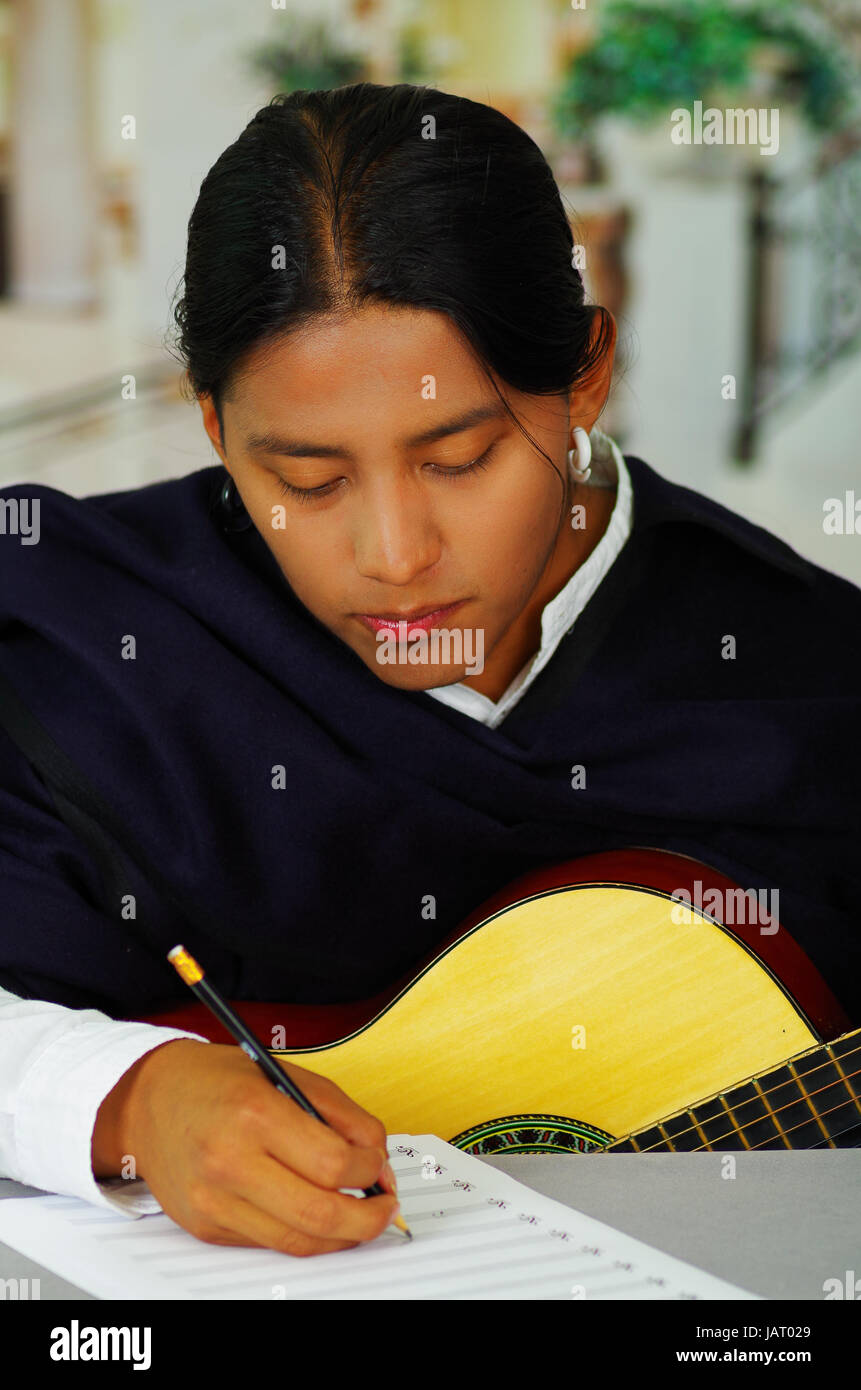 Indigenous young latin man writing notes to music with guitar, concept ...