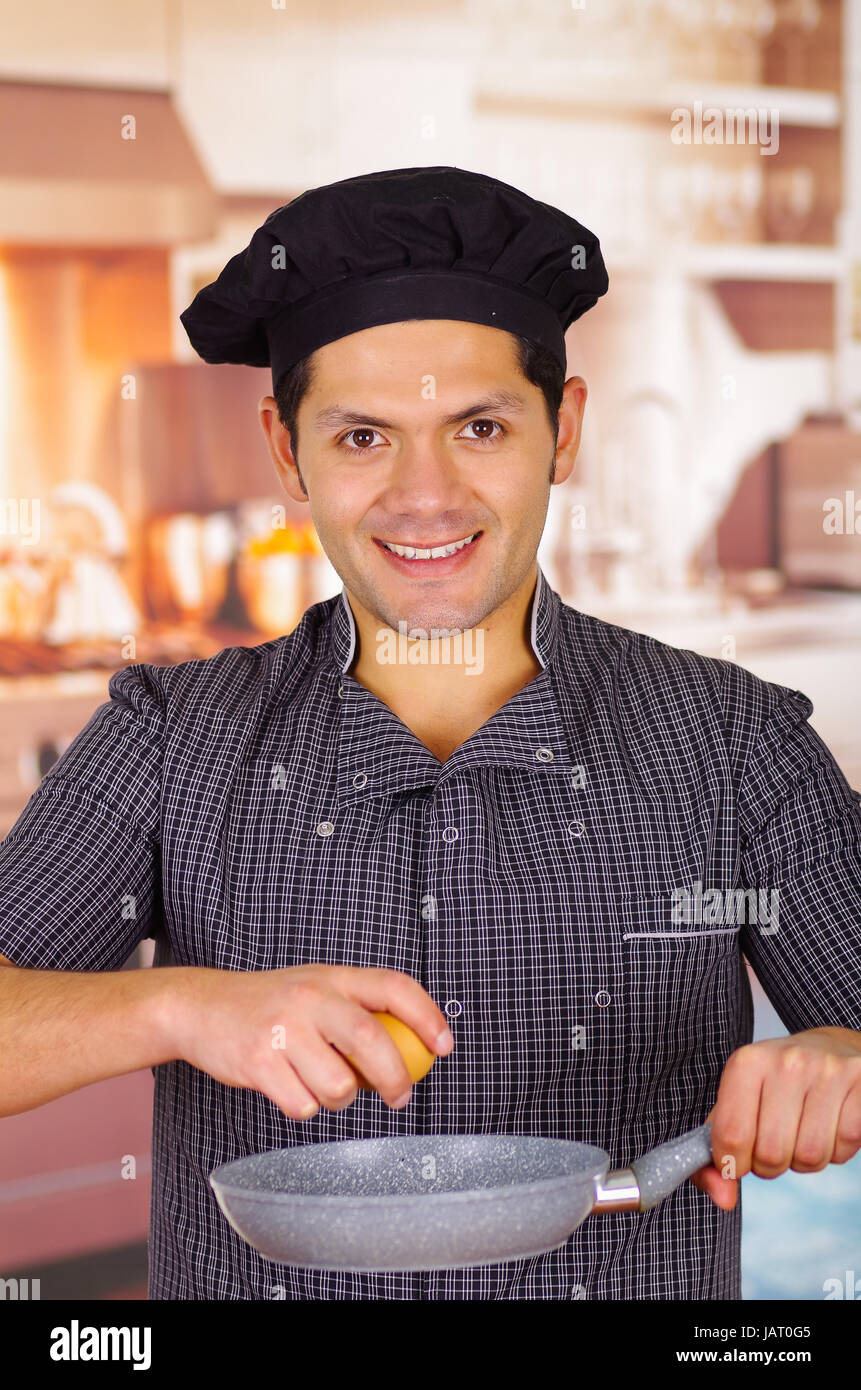 Smiling guy is holding a pan in kitchen with an egg in his hand cooking ...