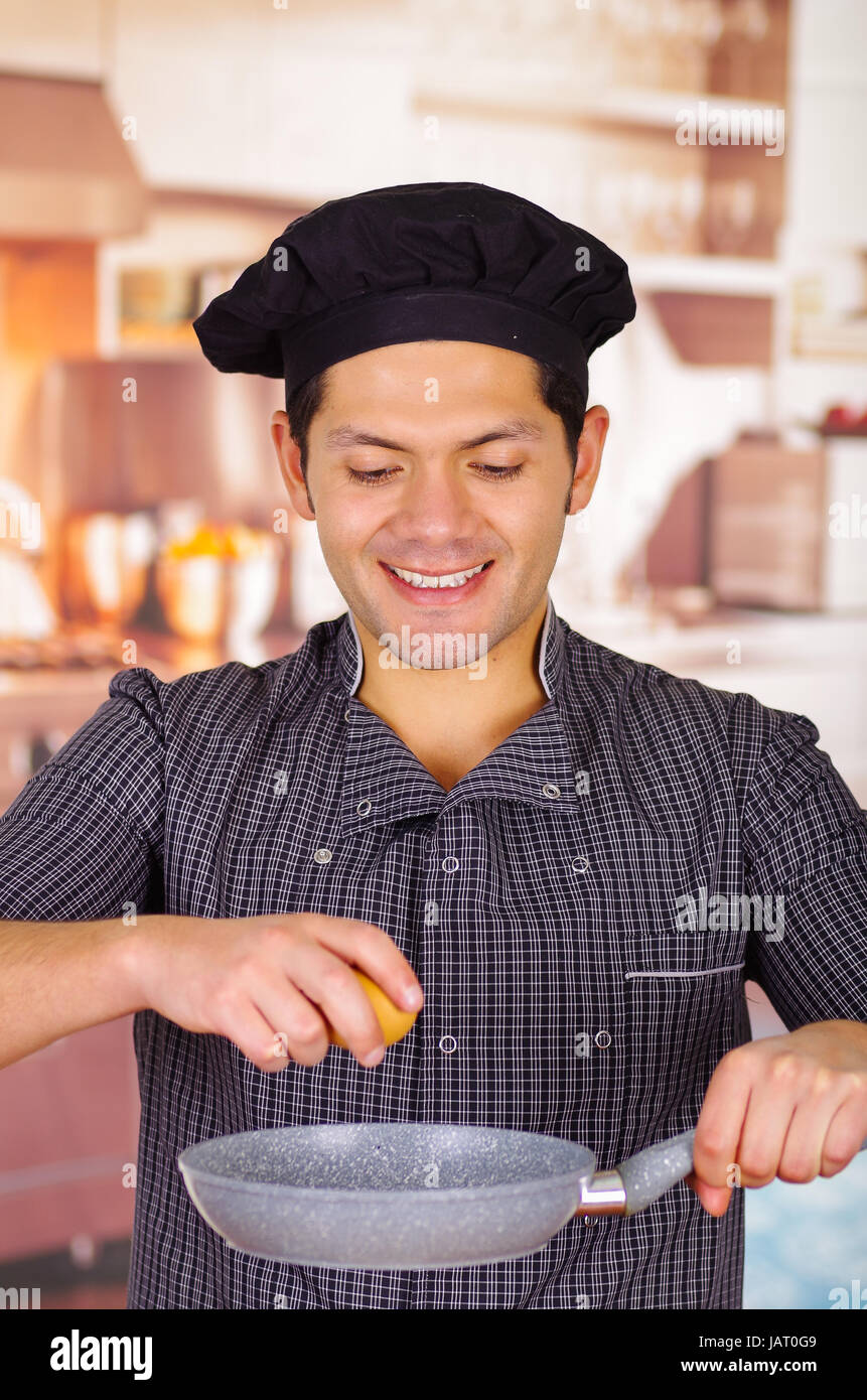 Smiling guy is holding a pan in kitchen with an egg in his hand cooking ...