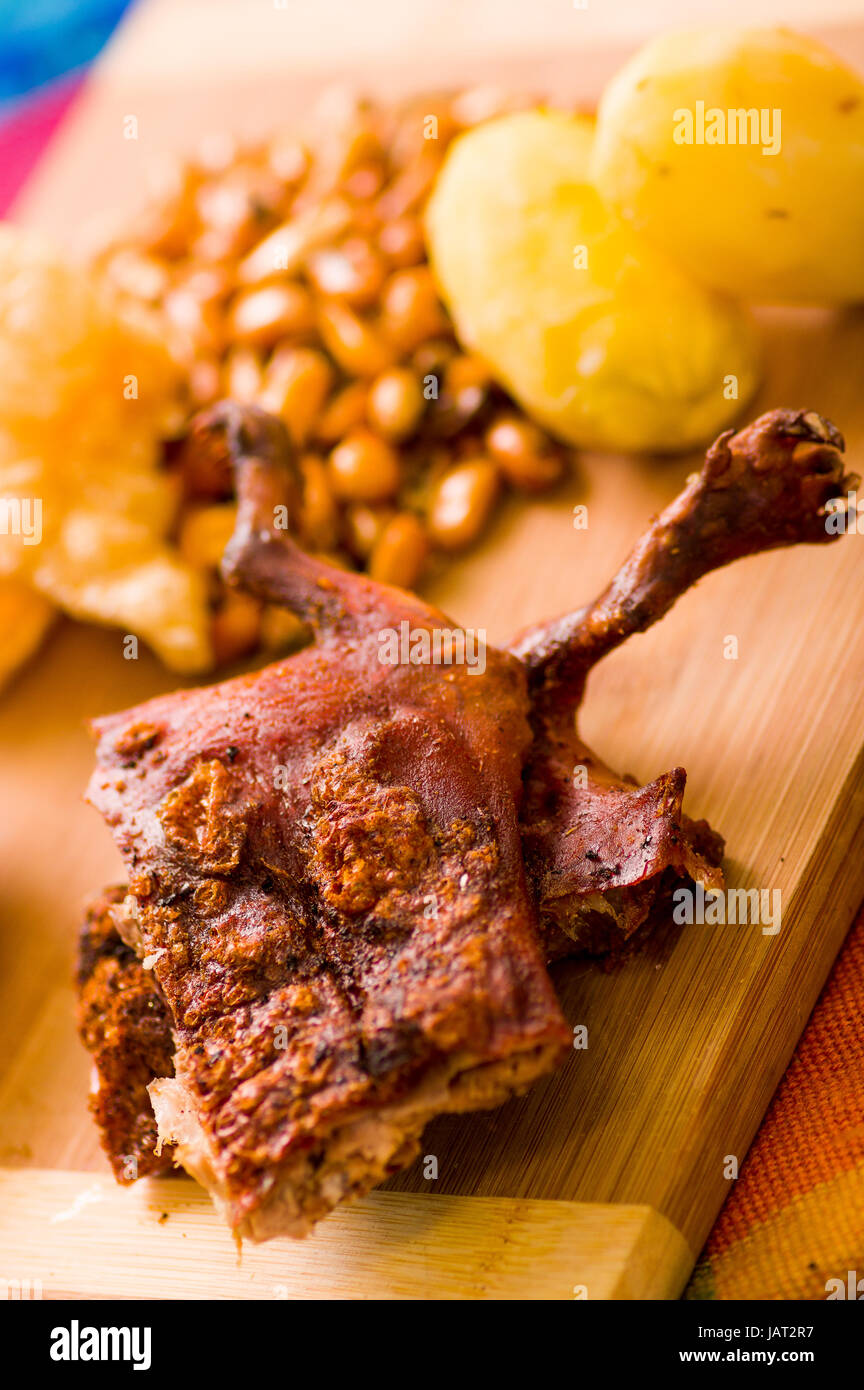 Cut pieces cooked guine pig meat lying on wooden surface next to ...